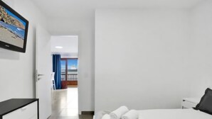 Quarto de hotel com uma cama, uma mesa de trabalho e uma televisão na parede.