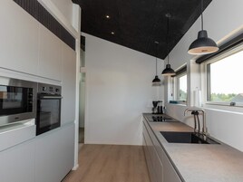 Cozinha moderna com eletrodomésticos embutidos, iluminação pendente e vista pela janela.