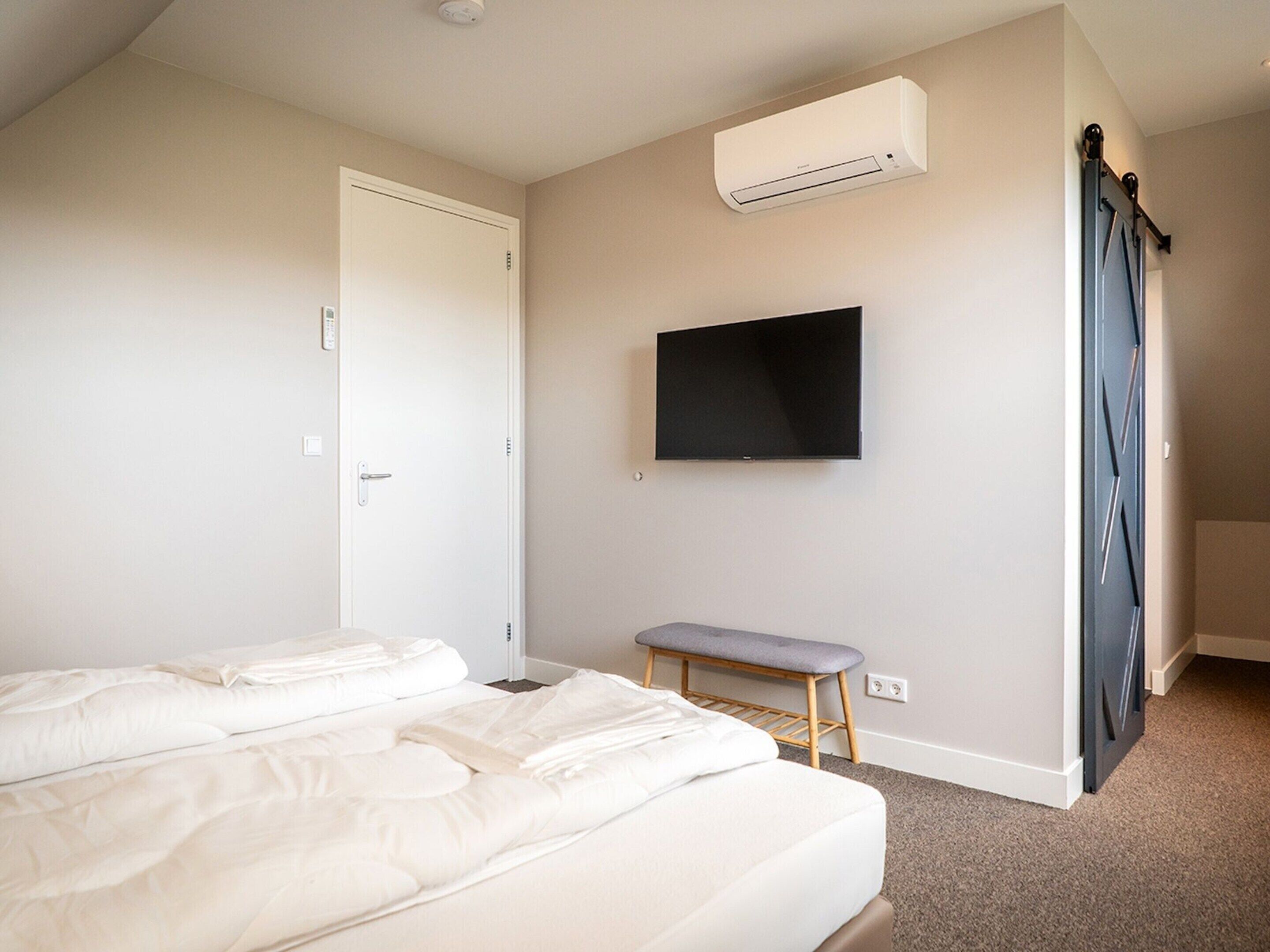 Quarto com cama, televisão na parede e ar condicionado.