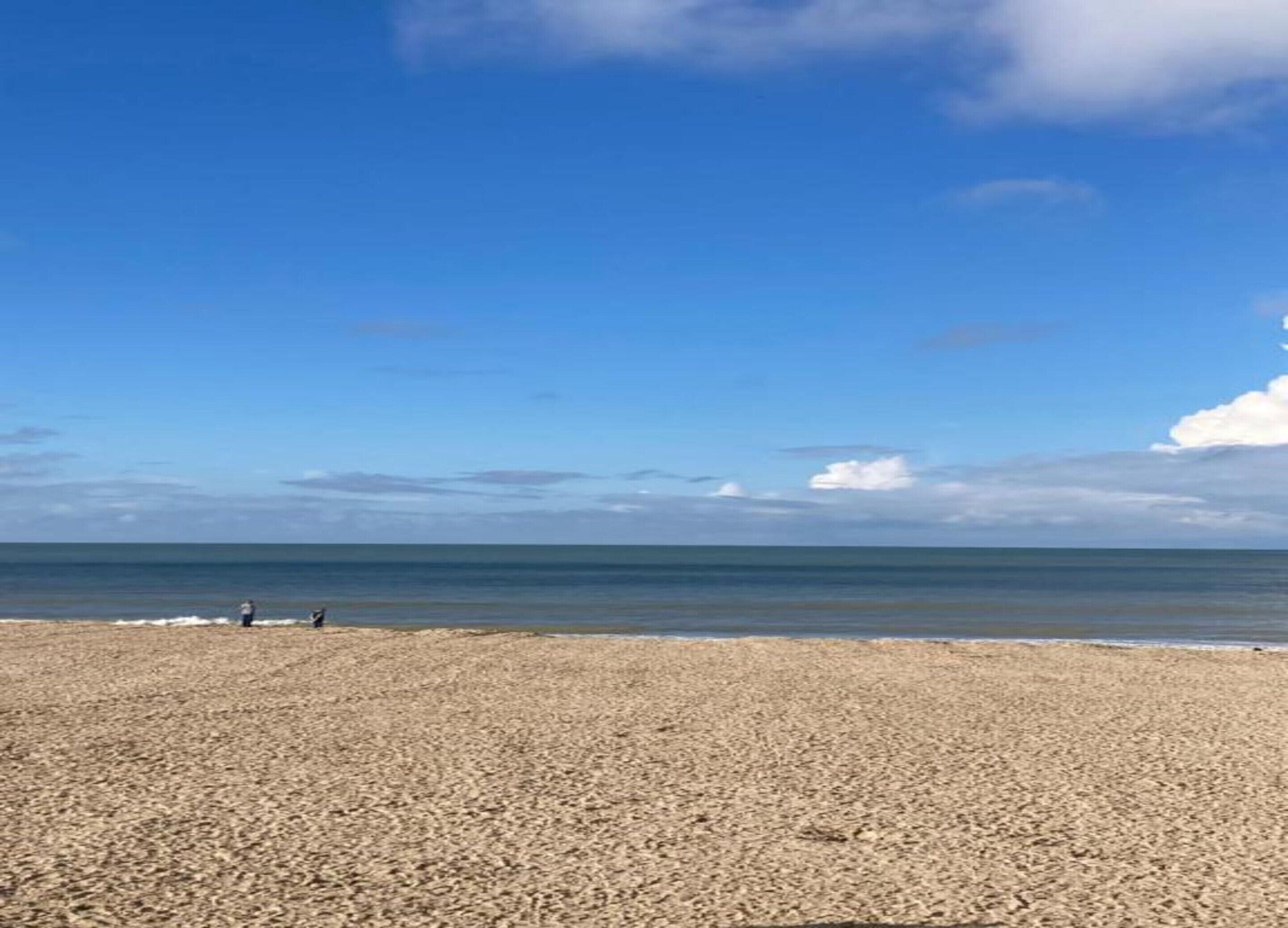 Uma praia com pedras, céu claro e águas calmas.