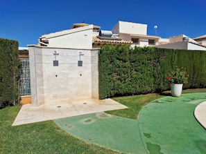 Um edifício moderno com telhado plano, uma pequena área fechada com piso ladrilhado e uma área externa verde com um vaso de planta.