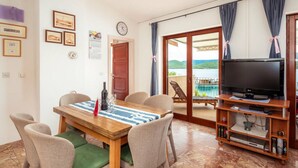 Uma sala de jantar com uma mesa, cadeiras e uma TV sobre um suporte de madeira.