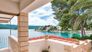 Varanda com parede de pedra, plantas em vasos e vista para um lago e edifícios.