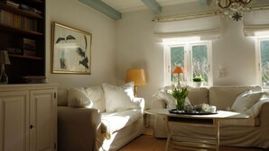 Uma sala de estar aconchegante, com um sofá branco, uma mesinha redonda e uma estante de livros.