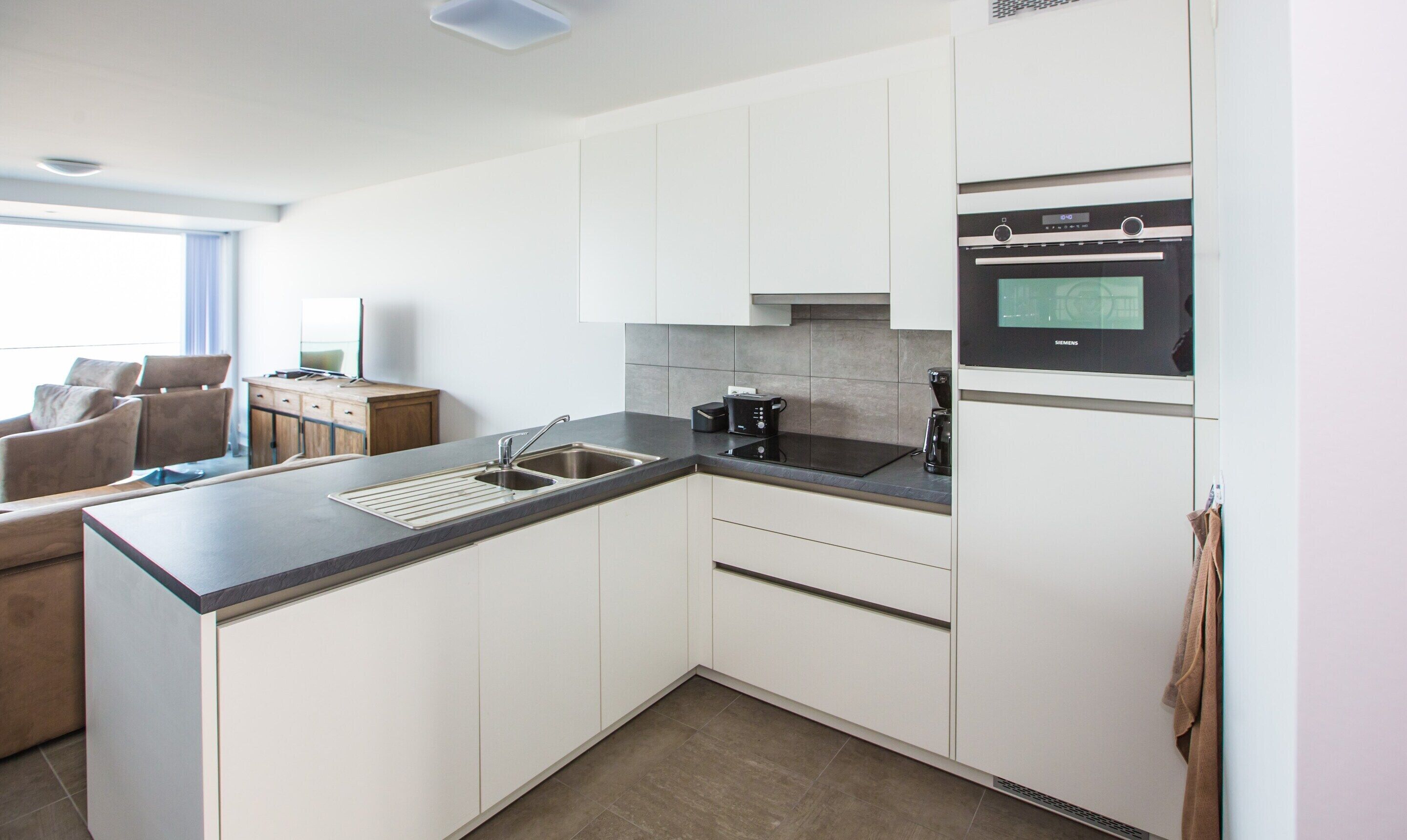 Uma cozinha moderna com armários brancos, bancada preta e um micro-ondas Siemens.