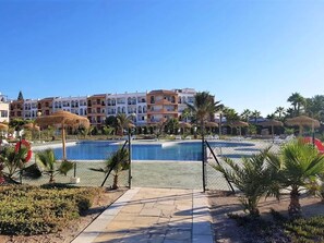 Um resort com piscina, palmeiras e edifícios altos com varandas.