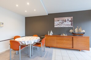 Uma sala de jantar com uma mesa redonda, cadeiras laranjas, um aparador de madeira e um quadro na parede.
