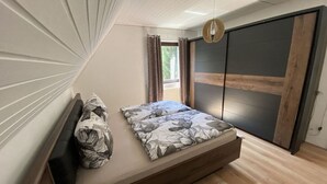 Quarto moderno com beliche, piso de madeira, uma janela grande com cortinas e uma porta deslizante.