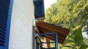 Uma passagem estreita que leva a uma porta de madeira, com uma parede branca e um batente de janela azul.