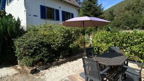 Uma casa com telhado de telhas, um pátio com mesa e cadeiras, e um grande guarda-sol.