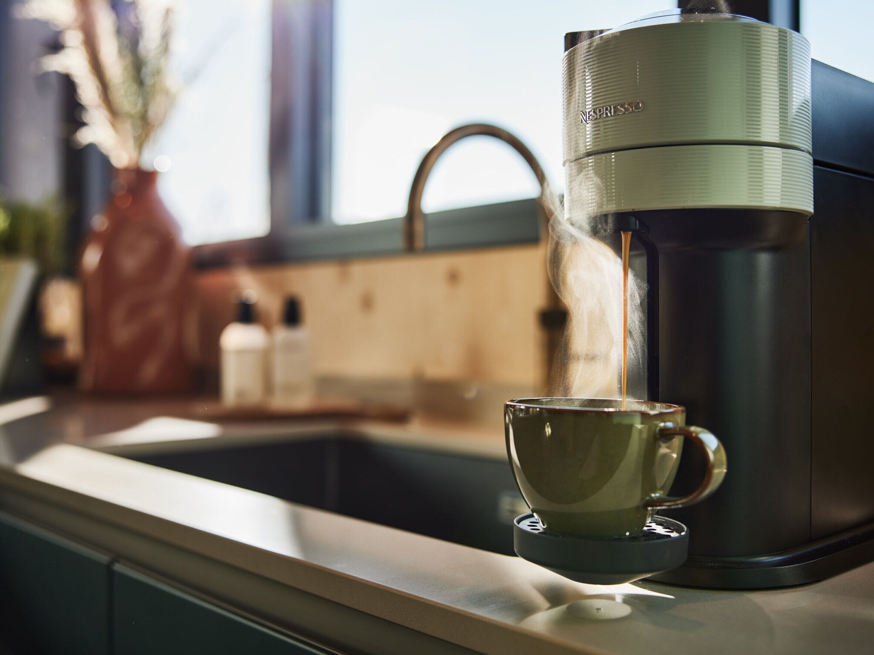 Uma cafeteira em uma bancada de cozinha, com uma xícara de café.