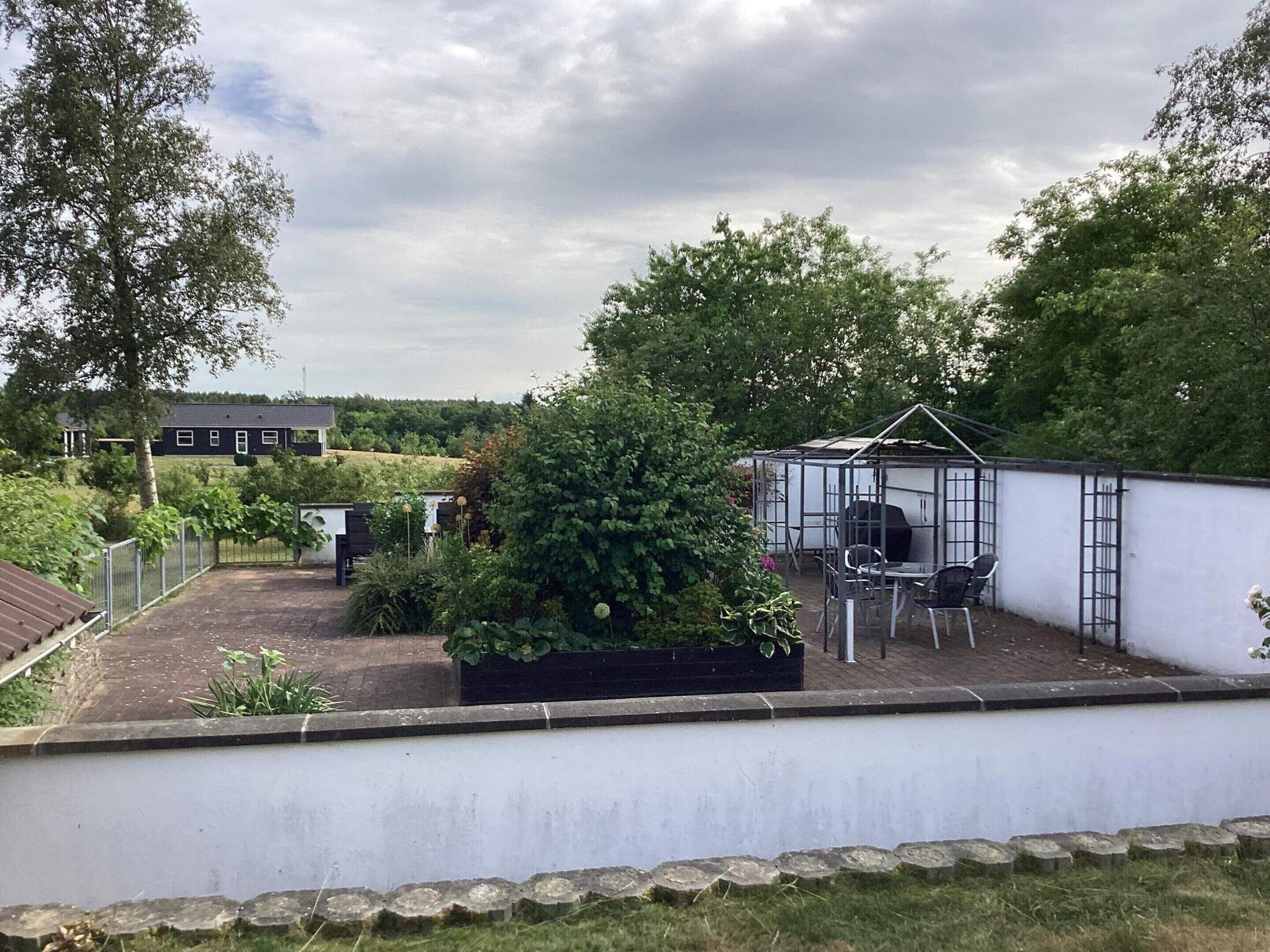 Um jardim com estufa, área de churrasco e pátio cercado.