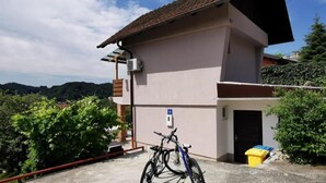Um edifício com telhado de telhas, uma bicicleta estacionada em frente e vista da vegetação e colinas ao redor.