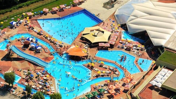 Vista aérea de um resort com várias piscinas, espreguiçadeiras, guarda-sóis e uma grande área coberta.
