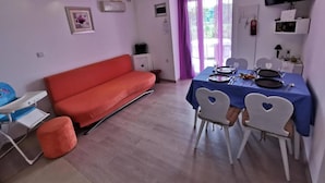 Quarto com sofá vermelho, mesa de jantar posta para dois e televisão na parede.