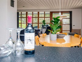 Uma sala de jantar com mesa redonda, cadeiras, garrafa de vinho, copos de vinho e uma planta em vaso.