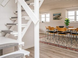 Interior moderno com escada branca, área de jantar com mesa e cadeiras, e uma grande janela com vista.