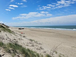Uma praia com uma duna, uma tenda vermelha e um objeto preto na areia.