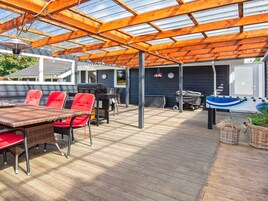 Um pátio externo com deck de madeira, uma mesa com cadeiras, churrasqueira e mesa de pebolim.