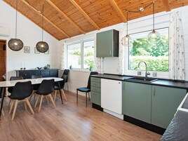 Cozinha moderna com vigas de madeira no teto, área de jantar com mesa e cadeiras, e janela com vista para o verde.