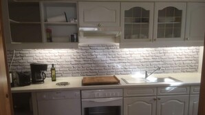 Uma cozinha com armários brancos, painel de parede de tijolos, cafeteira, tábua de corte e lava-louças.