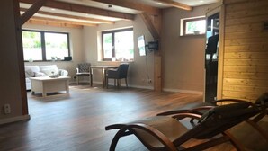 Uma sala de estar ampla com piso de madeira, um sofá, uma mesa de jantar com cadeiras e uma parede de madeira.
