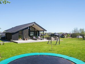 Uma casa moderna com varanda coberta, trampolim e um pequeno jardim.