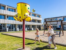 Um parquinho com um brinquedo de escalada amarelo, uma rede de voleibol e balanços.