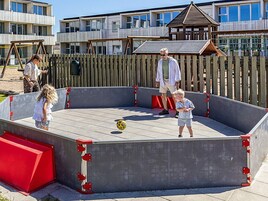Área de recreação infantil com estrutura de concreto, cerca de madeira e um edifício ao fundo.