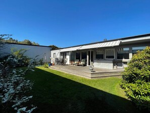 Uma casa moderna térrea com varanda coberta, churrasqueira e um pequeno jardim.