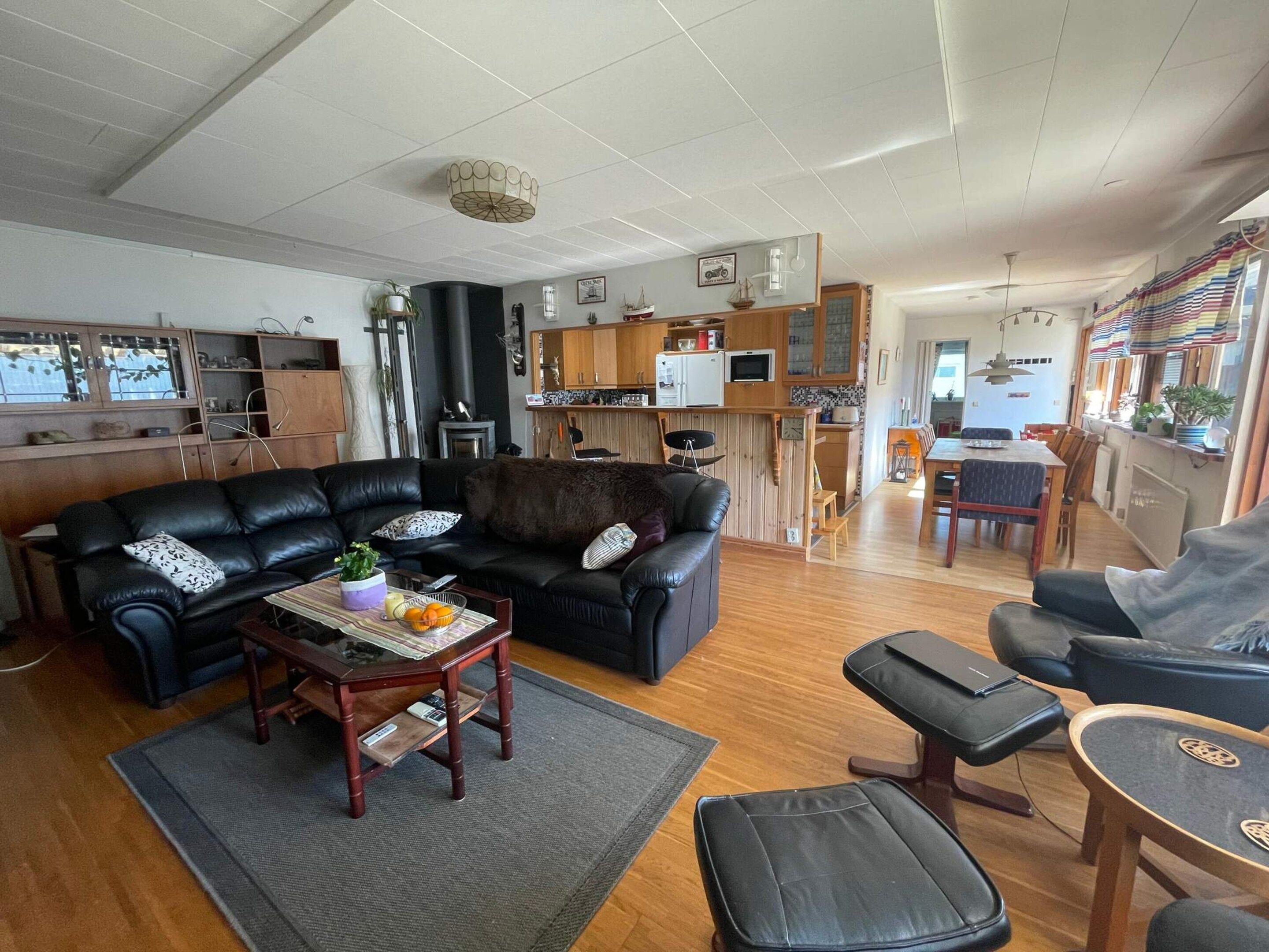 Uma sala de estar moderna com um sofá seccional, uma mesa de centro e um espaço de jantar com mesa e cadeiras de madeira.
