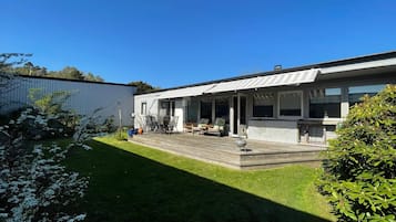 Uma casa moderna com varanda coberta, churrasqueira e gramado bem cuidado.