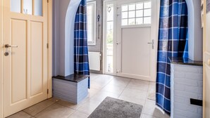 Um corredor com uma porta branca, uma janela com moldura branca e uma cortina quadriculada azul e branca.