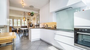 Uma cozinha moderna com armários brancos, forno embutido e área de refeições com mesa e cadeiras de madeira.