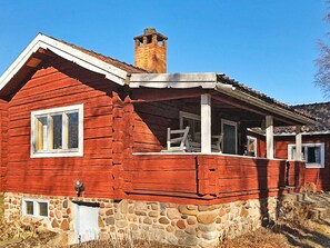 Uma casa de madeira vermelha com base de pedra, chaminé e varanda.