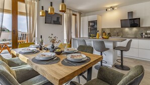 Uma sala de jantar moderna com uma mesa de madeira, cadeiras estofadas cinzas e uma cozinha ao fundo.