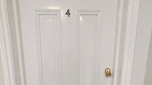 Uma porta branca com puxador de latão e uma pequena placa de número de latão acima.