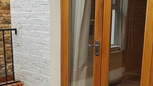 Uma porta de madeira com painéis de vidro, uma parede de tijolos brancos e um chão de concreto com manchas.