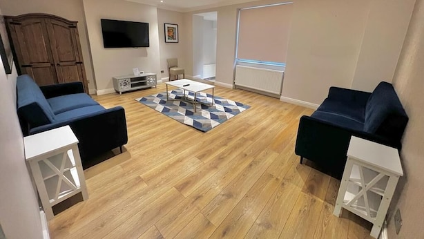 Uma sala de estar moderna com dois sofás escuros, uma mesa de centro e uma TV fixada na parede.
