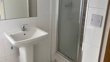 Casa de banho com lavatório assentado, espelho e cabine de duche em vidro.