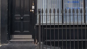Um edifício com moldura preta, porta numerada, grade de metal e janela com cortina.