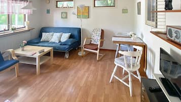 Uma sala de estar acolhedora com sofá, cadeiras, mesa, televisão e janela com cortinas.