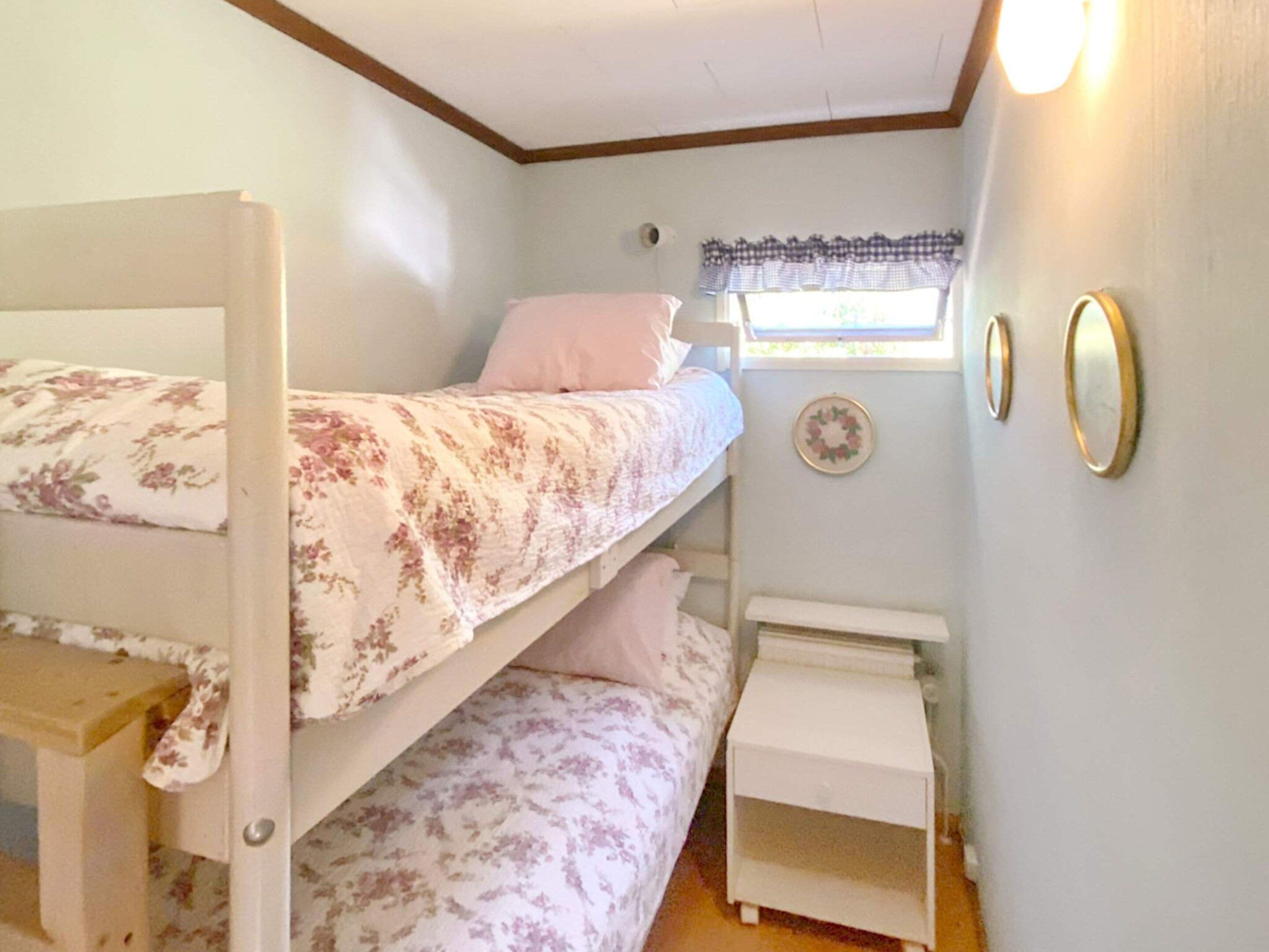 Quarto com beliche, janela, mesinha e decorações nas paredes.