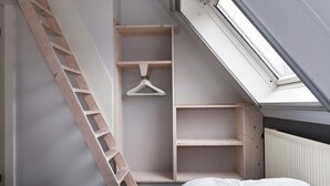 Quarto com claraboia, escada de madeira e armário com prateleiras e cabideiro.