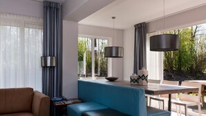 Uma sala de estar moderna com um sofá, um banquinho azul, uma mesa de jantar com cadeiras e uma janela grande com cortinas.