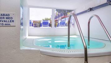 Uma piscina coberta pequena com parede de vidro, escada de metal e aviso indicando tempo de espera de 15 minutos.