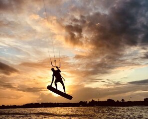 Silhueta de uma pessoa praticando kitesurf contra um céu de pôr do sol.