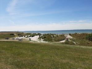 Paisagem costeira com um caminho de areia, bicicletas e um farol ao longe.