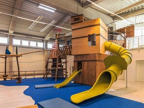 Um parquinho com escorregador, estruturas de escalada e piso coberto por carpete azul.