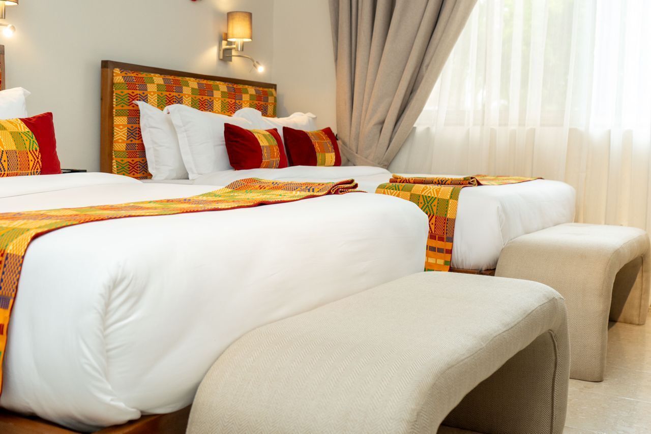 Quarto de hotel com uma cama grande, duas mesas de cabeceira e cabeceira estampada com um padrão colorido.